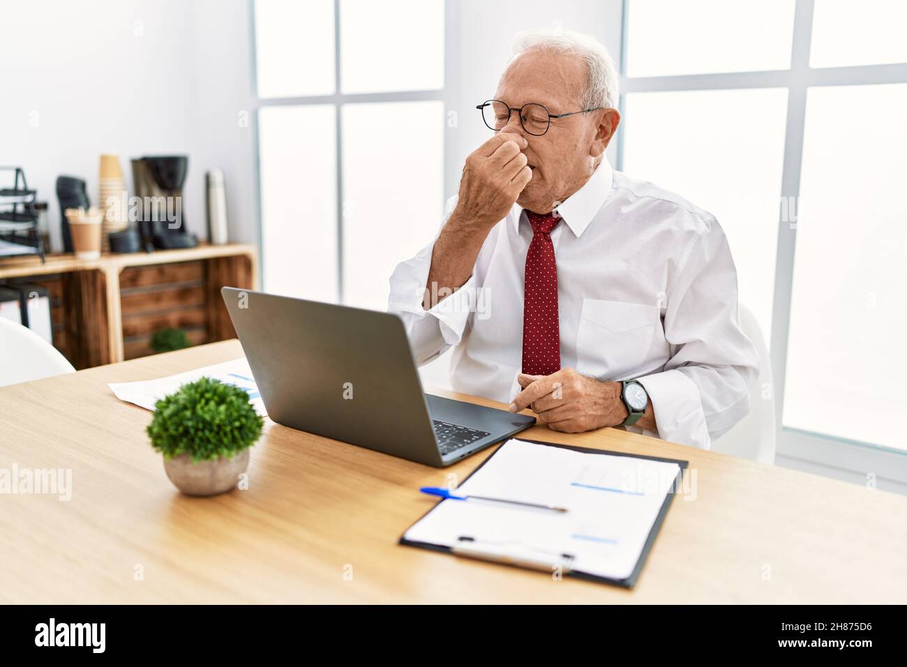 Senior man working at the office using computer laptop smelling ...