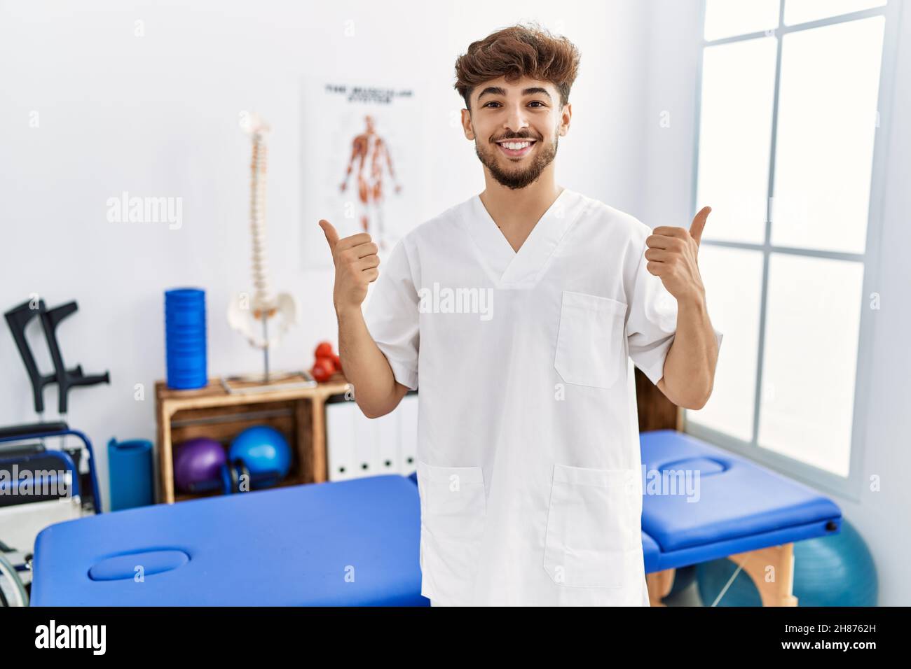 Young arab man working at pain recovery clinic success sign doing ...