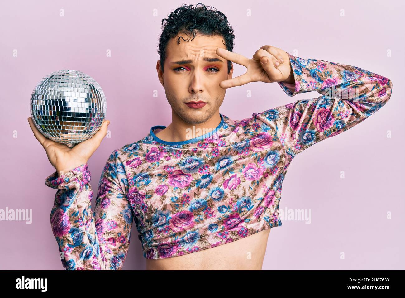 Handsome man wearing make up holding shiny disco ball depressed and ...