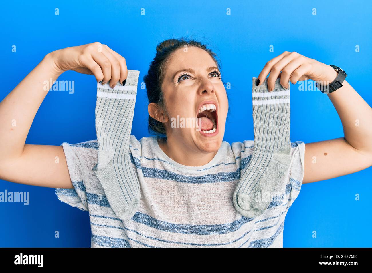 Young blonde woman holding socks angry and mad screaming frustrated and ...
