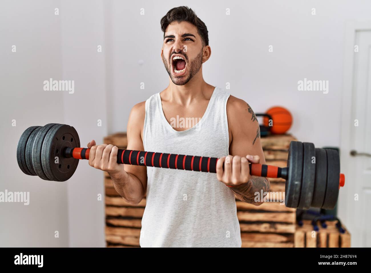 Young hispanic man training with weighs angry and mad screaming ...