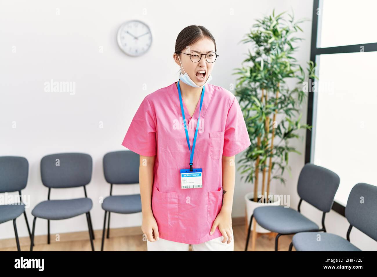 Young asian nurse woman at medical waiting room angry and mad screaming ...