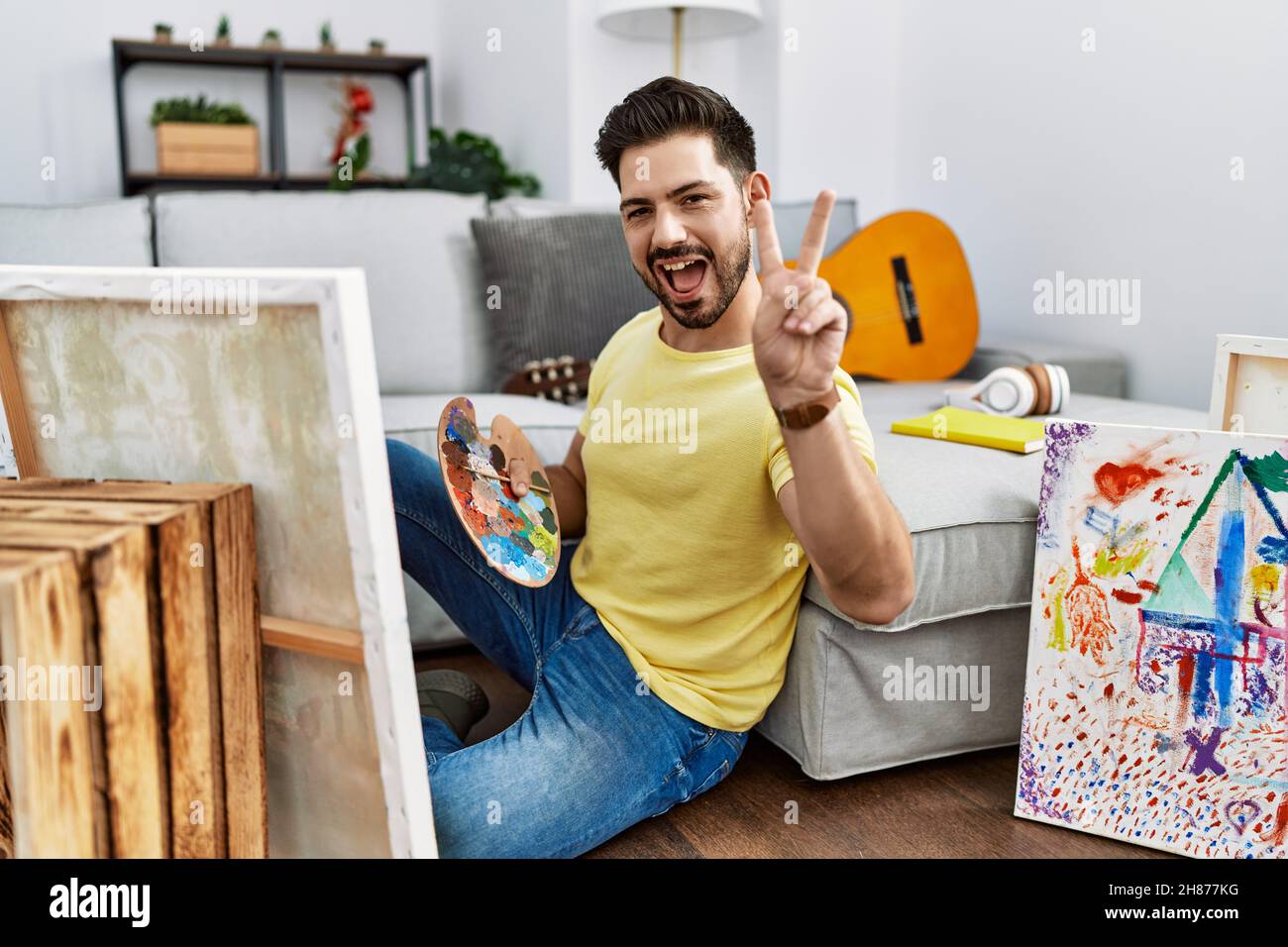 Young man with beard painting canvas at home smiling with happy face ...