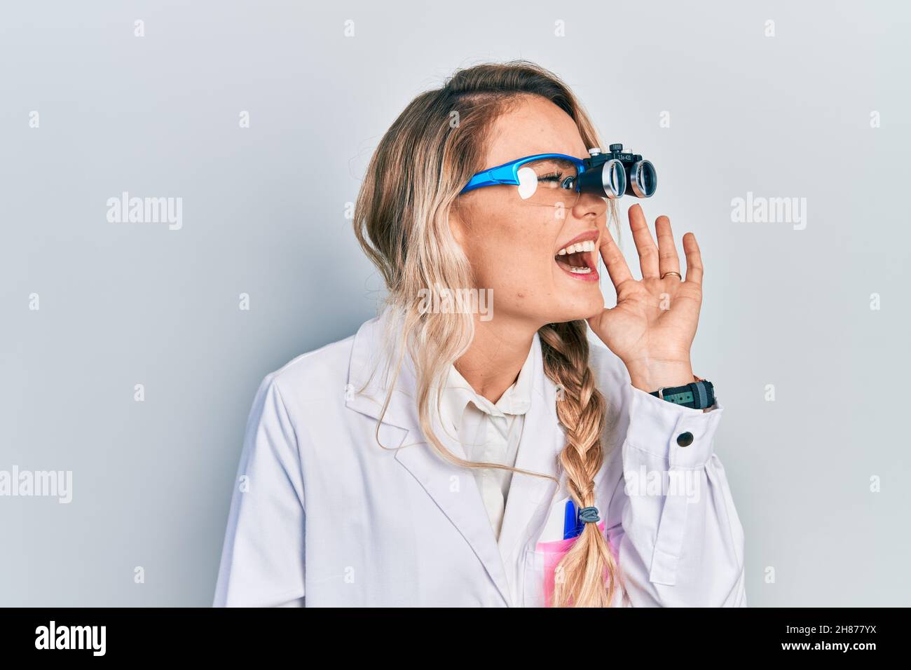 Beautiful young blonde woman wearing optometry glasses shouting and screaming loud to side with ...