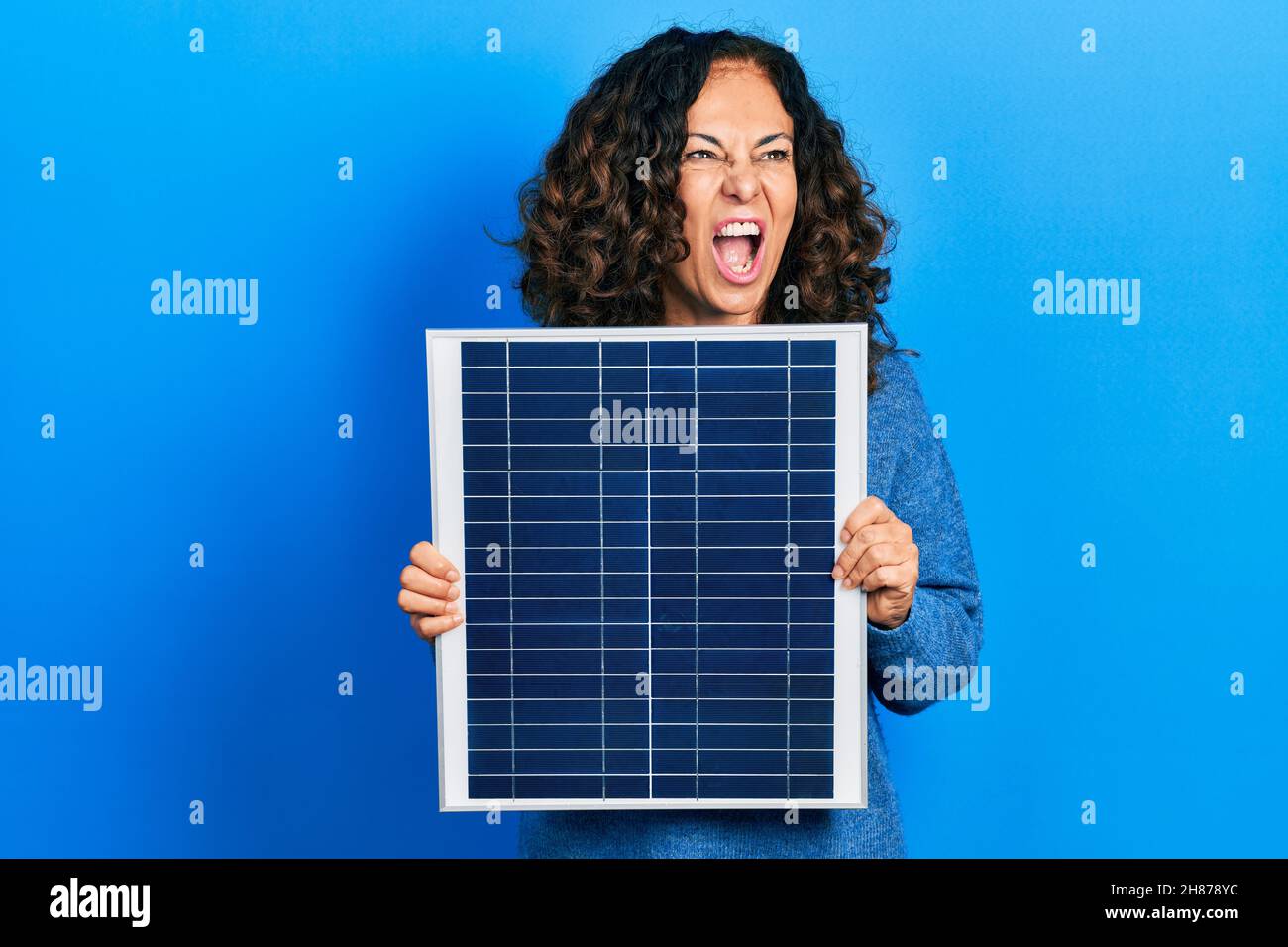 Middle age hispanic woman holding photovoltaic solar panel angry and ...