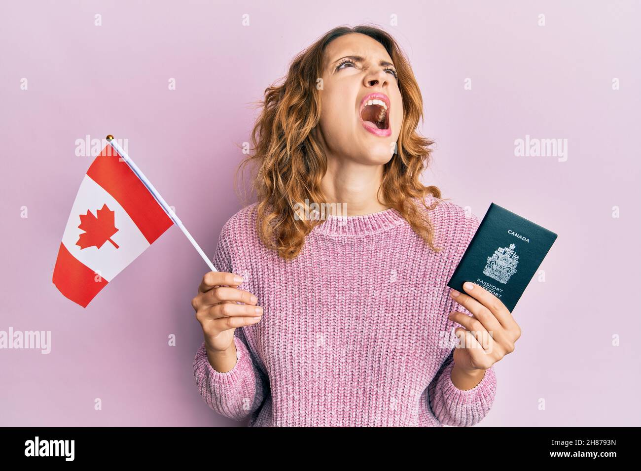 Young caucasian woman holding canada flag and passport angry and mad ...