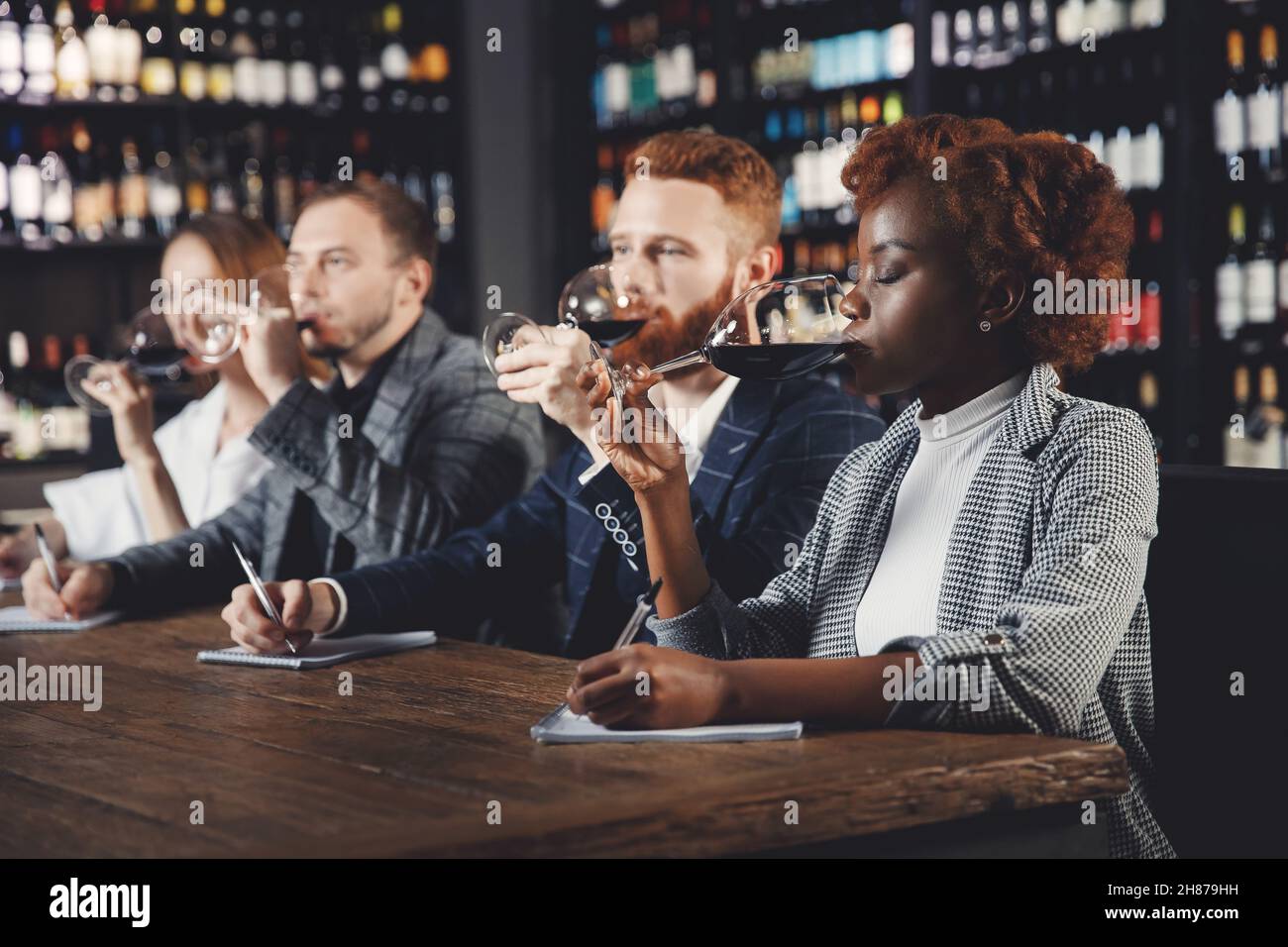 African Woman and caucasian man sommeliers tasting red wine and taking ...