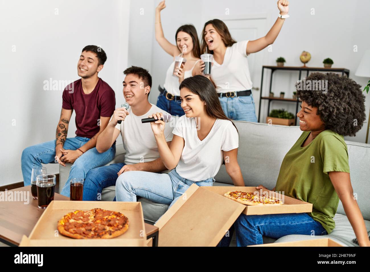 Group of young friends having party eating italian pizza and singing ...