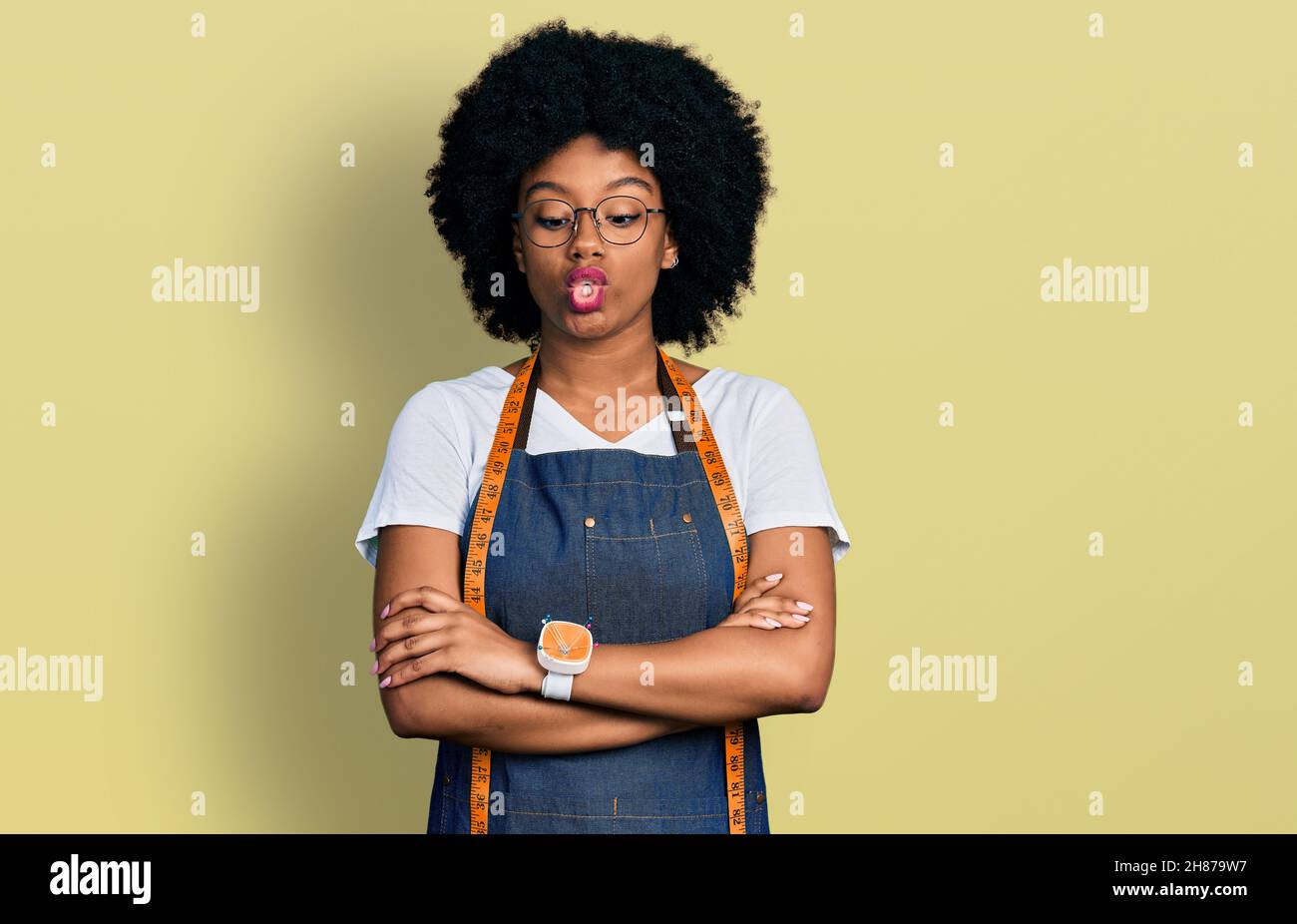 Young african american woman dressmaker designer wearing atelier apron making fish face with ...