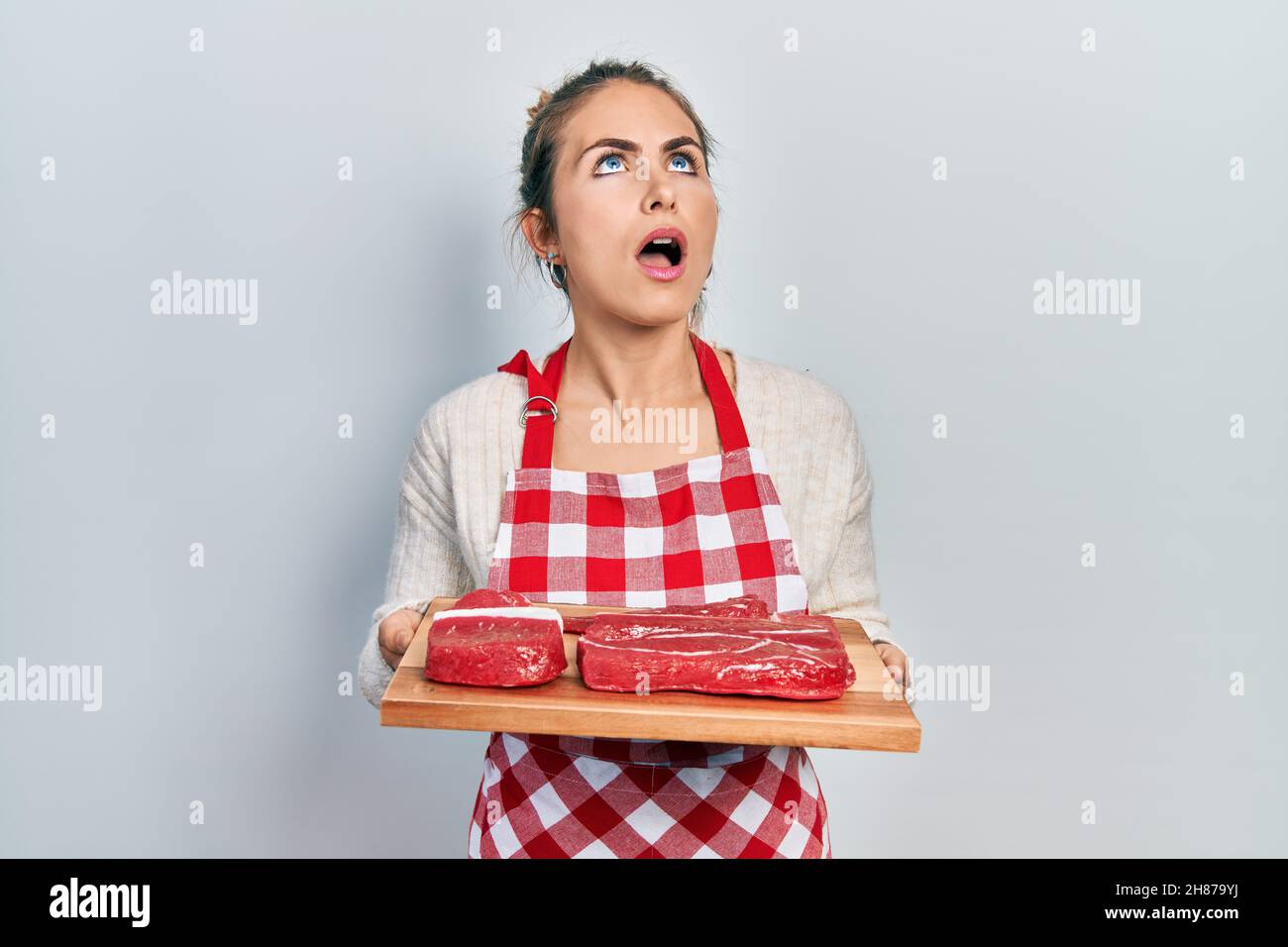 Young caucasian woman holding board with raw meat angry and mad ...