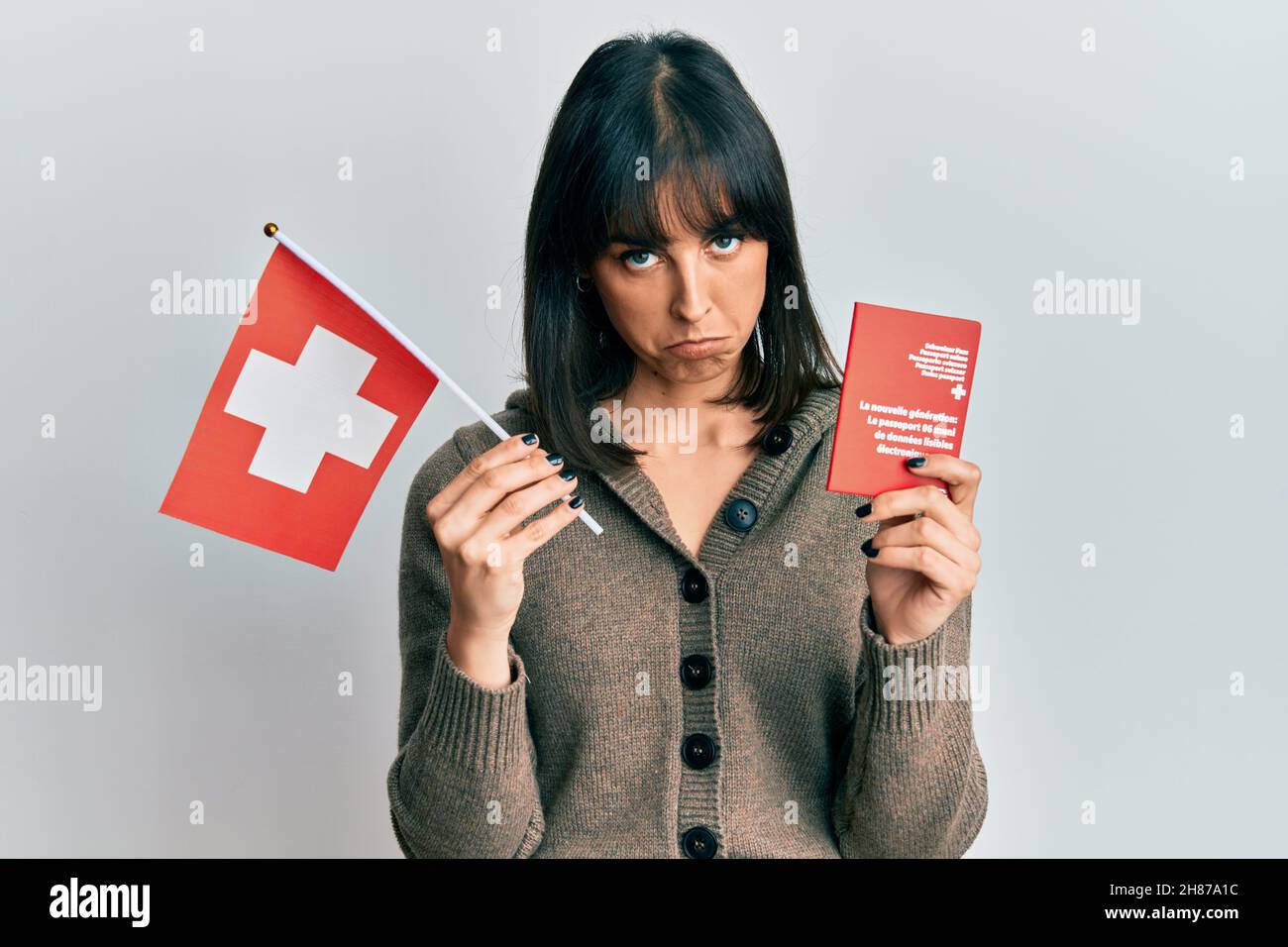 Young hispanic woman holding swiss flag and passport depressed and ...