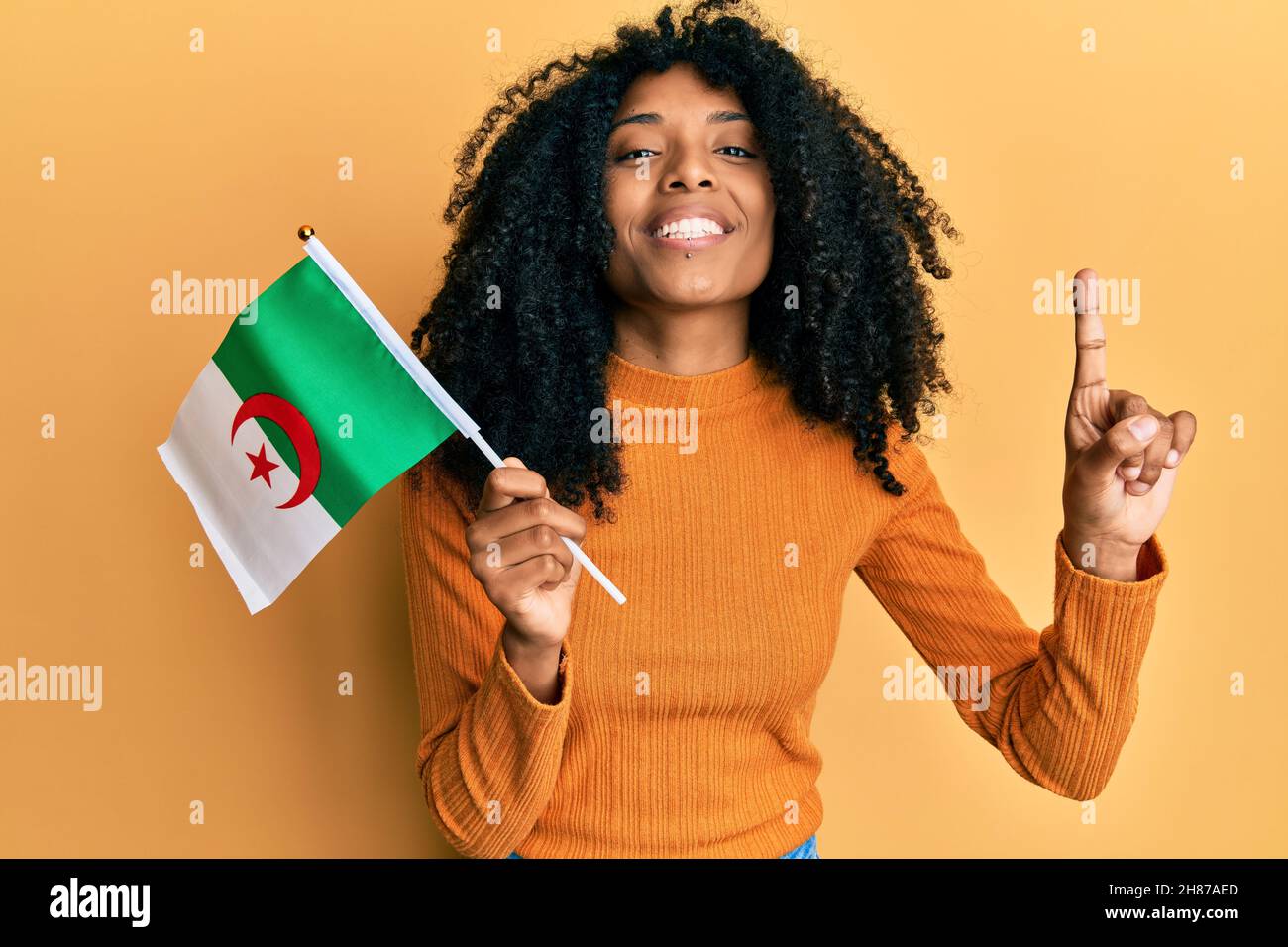 African american woman with afro hair holding algeria flag smiling with ...