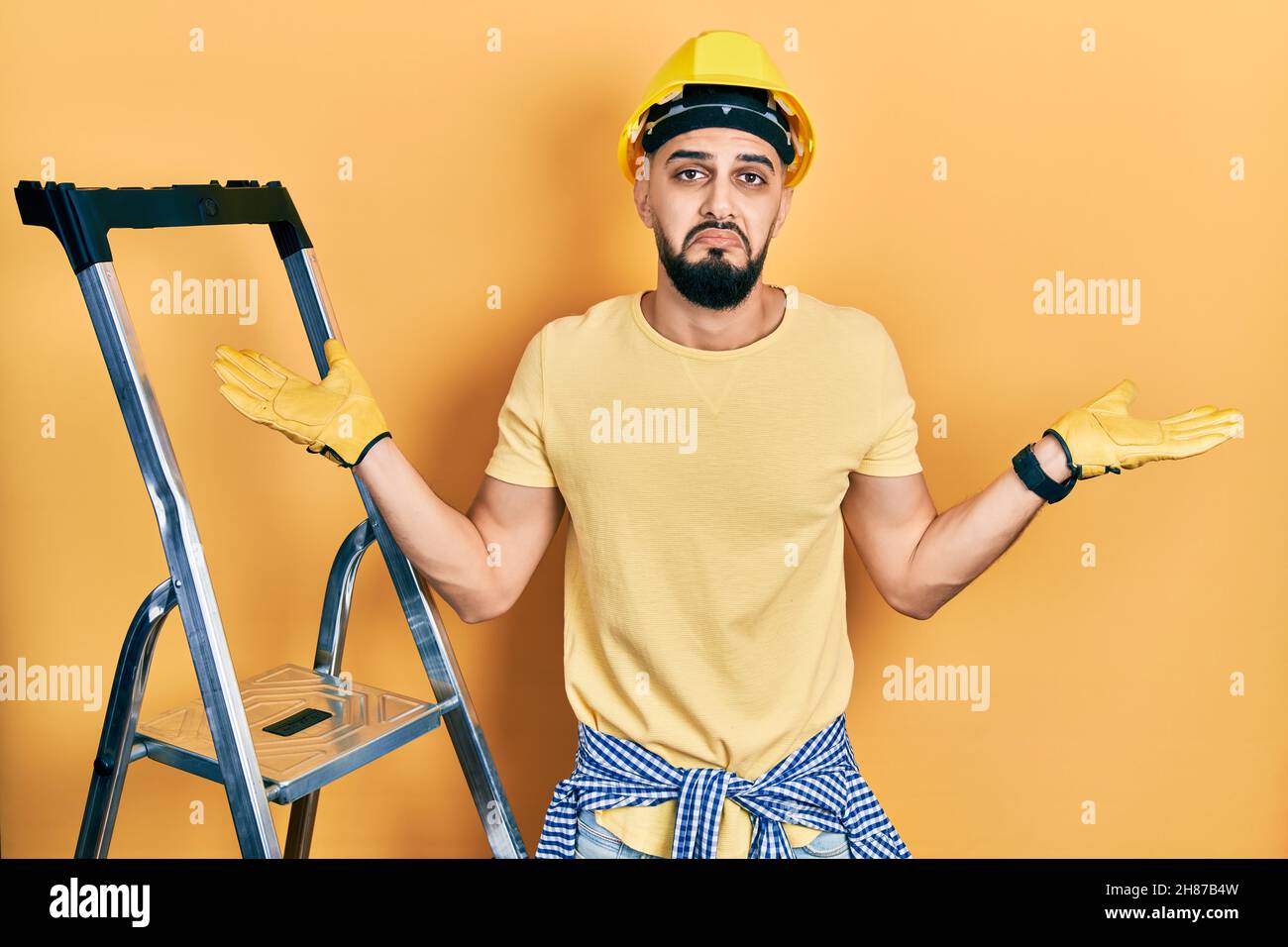 Handsome man with beard by construction stairs wearing hardhat clueless ...