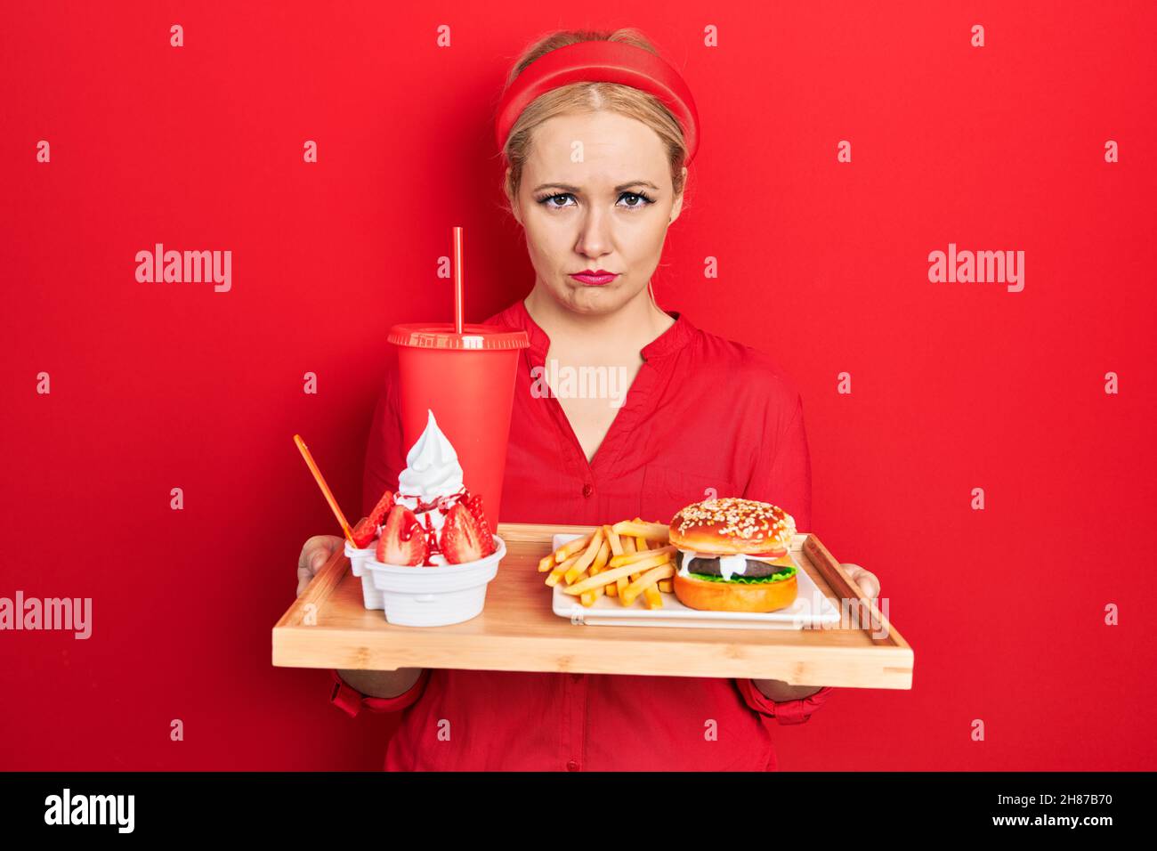 Young blonde woman eating a tasty classic burger with fries and soda ...