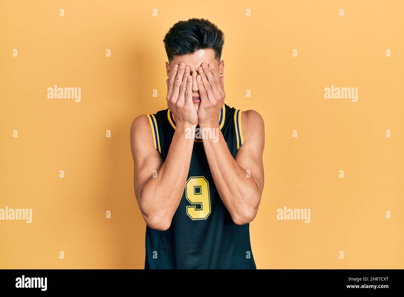 Young hispanic man wearing basketball uniform with sad expression ...