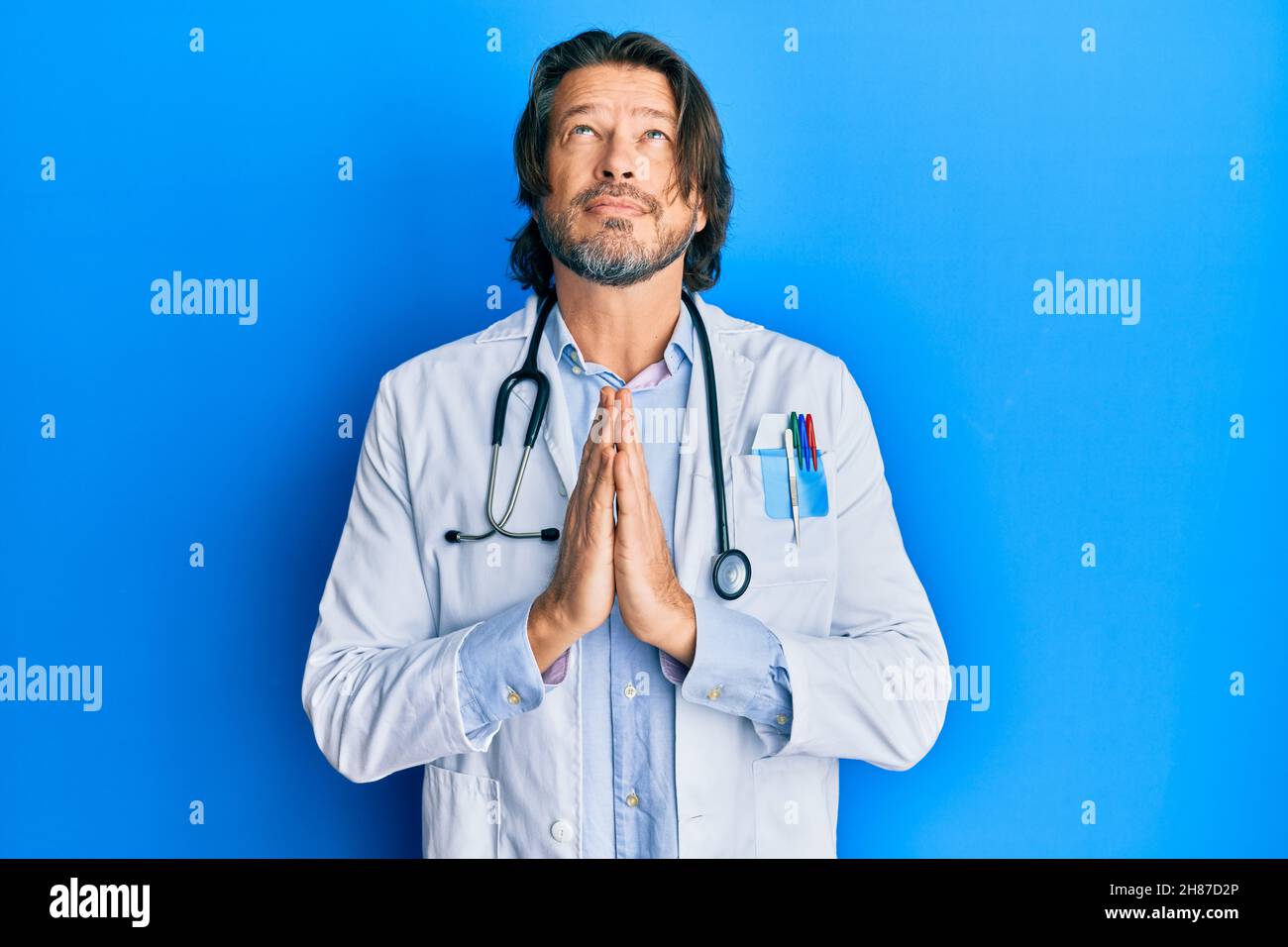 Middle age handsome man wearing doctor uniform and stethoscope begging ...