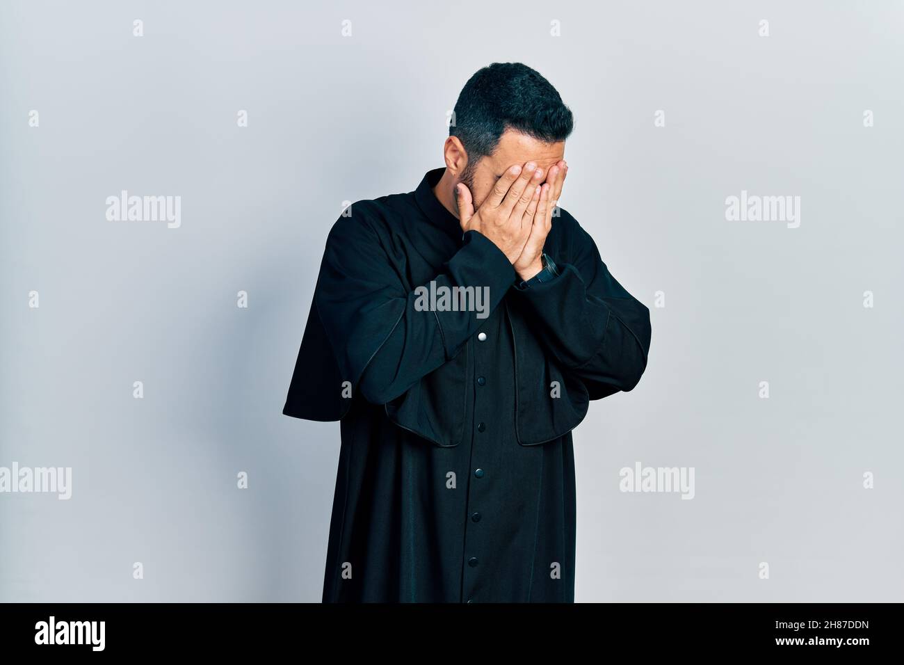 Handsome hispanic man with beard wearing catholic priest robe with sad ...