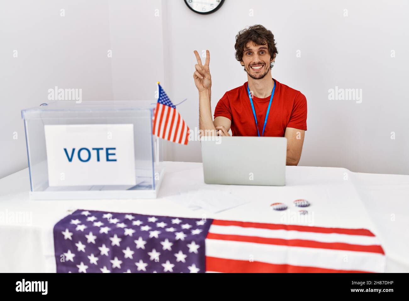 Young hispanic man at political election sitting by ballot smiling with ...