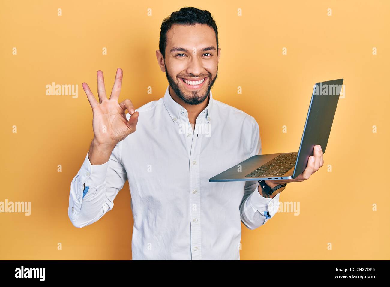 Hispanic man with beard working using computer laptop doing ok sign ...
