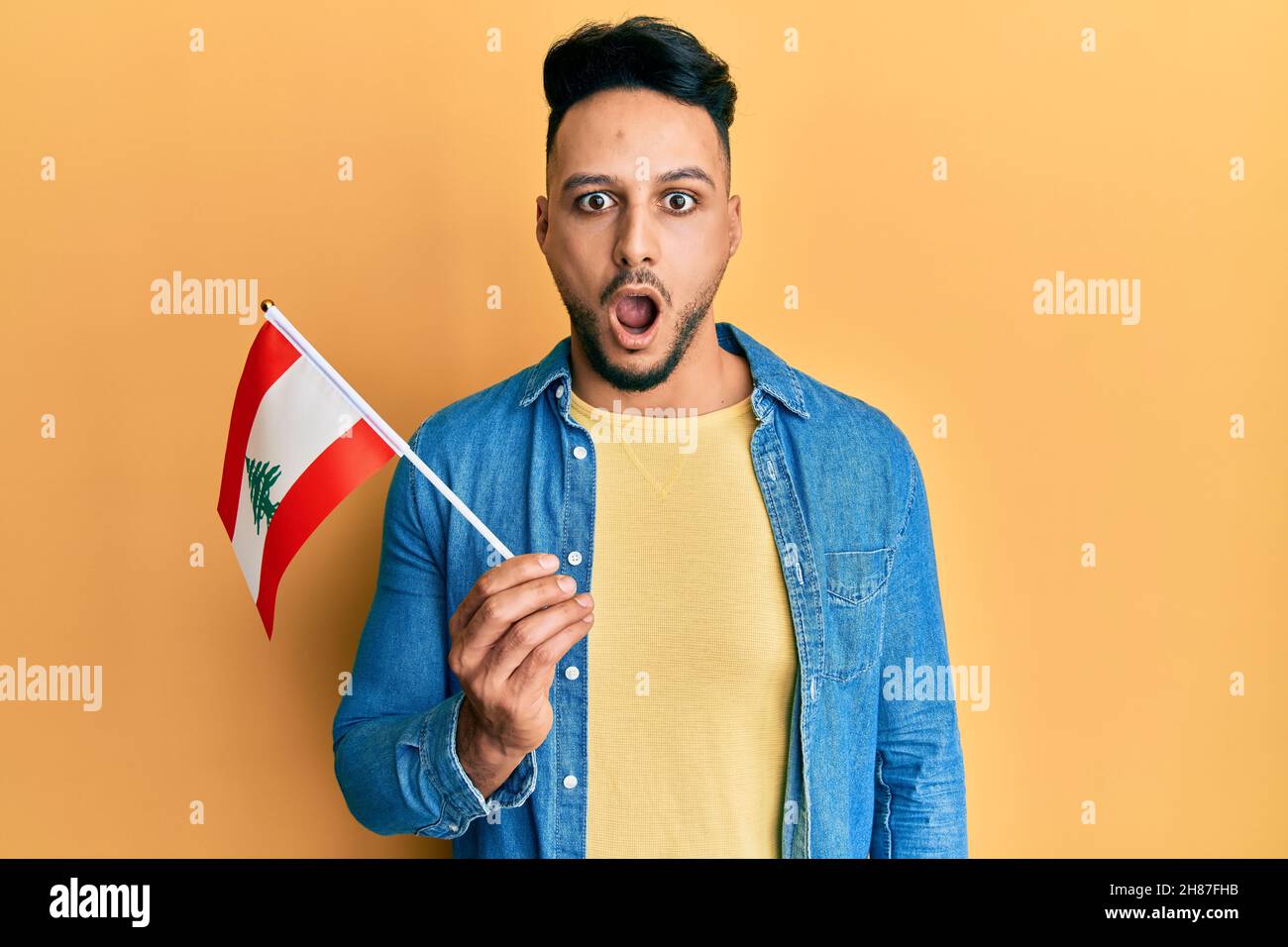 Young arab man holding lebanon flag scared and amazed with open mouth ...
