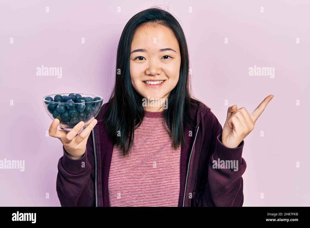 Young chinese girl holding blueberries smiling happy pointing with hand ...