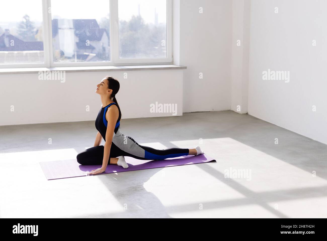 Smiling woman performing pose at bright studio. Flexible lady in yoga ...