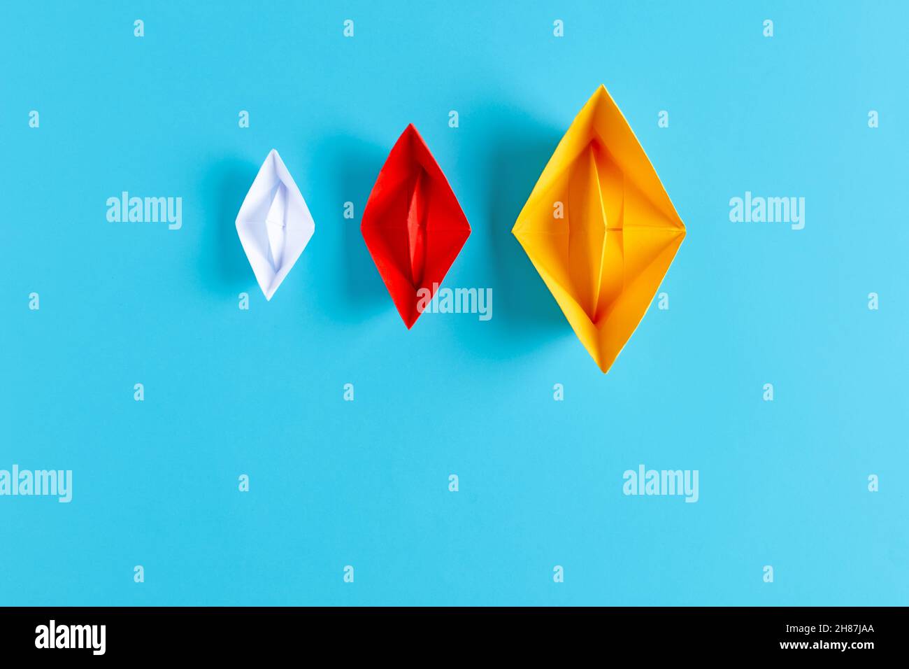 Three paper boats with different size and colors on blue background ...