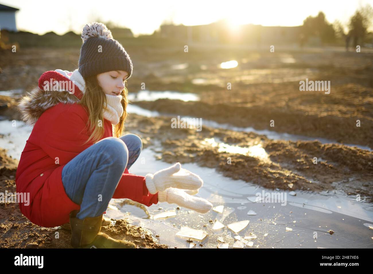 Happy young girl playing with thin ice puddles formed on the frozen ...