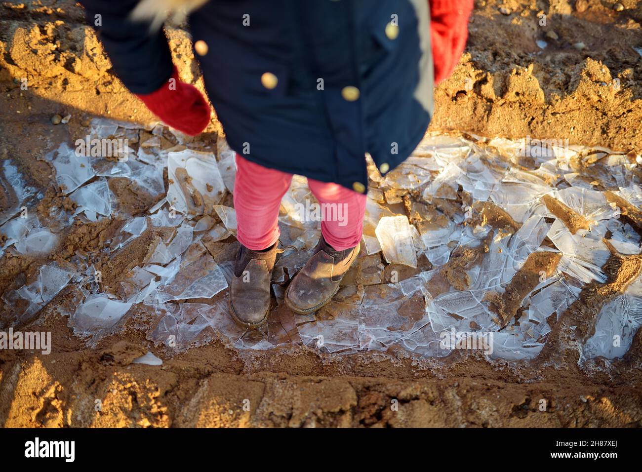 Happy young girl playing with thin ice puddles formed on the frozen ...