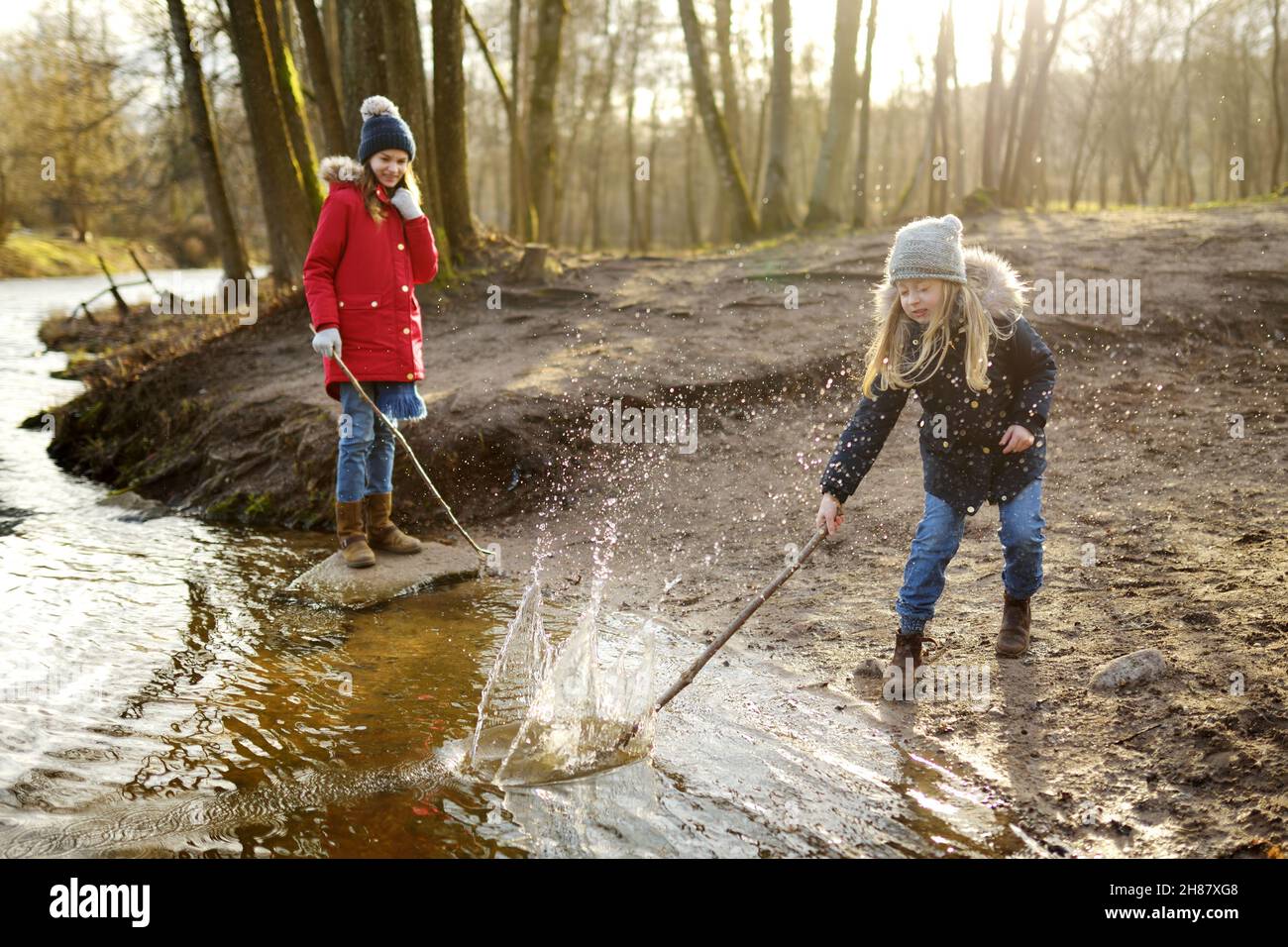 Two cute young sisters having fun by a river on warm spring day ...