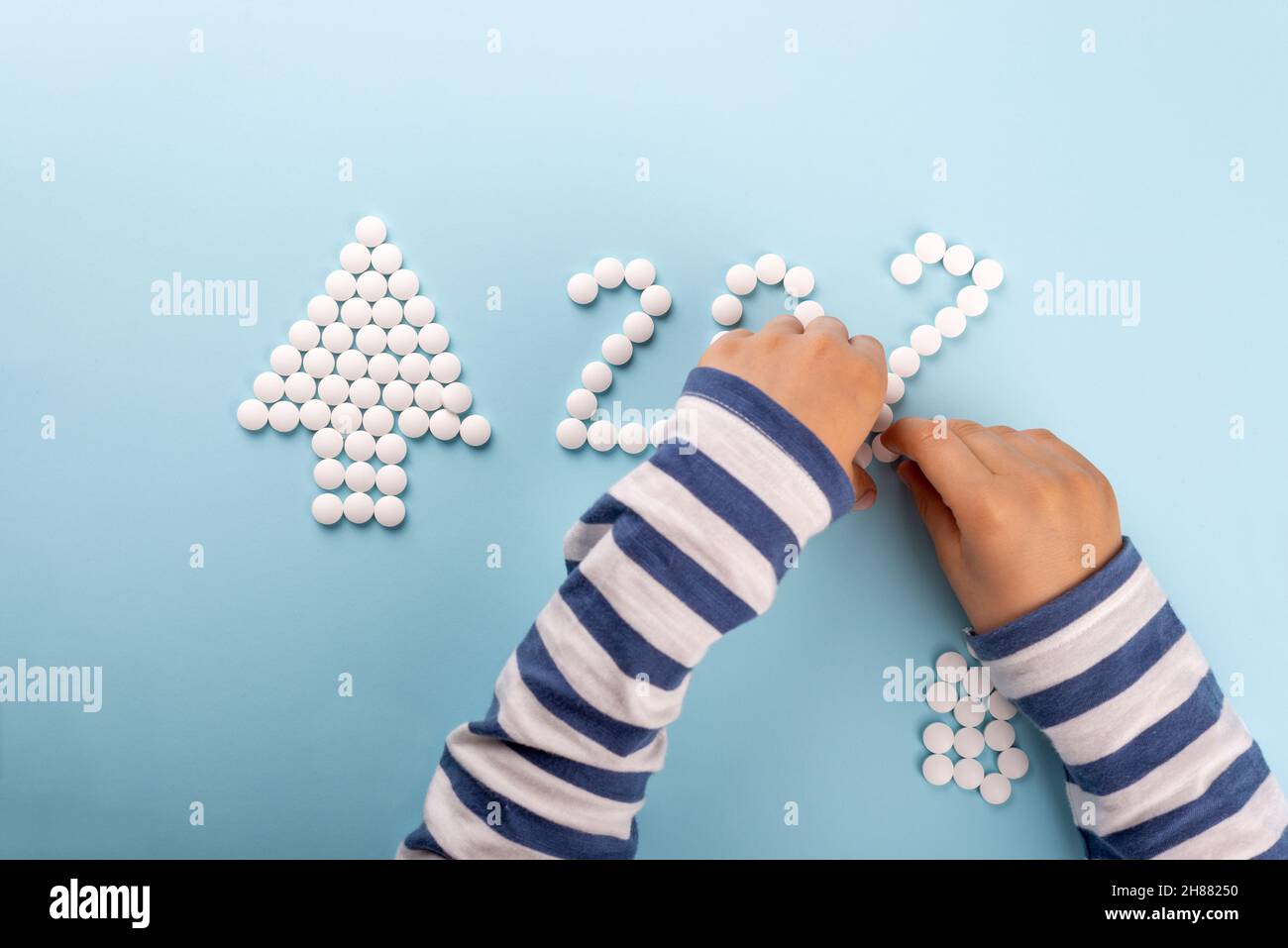 Boy's hands making 2022 and Christmas tree from white medication pills ...