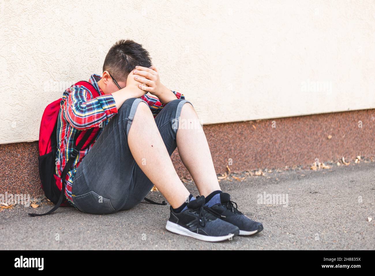 Lonely boy sitting alone on the ground, isolated from his peers, hiding ...