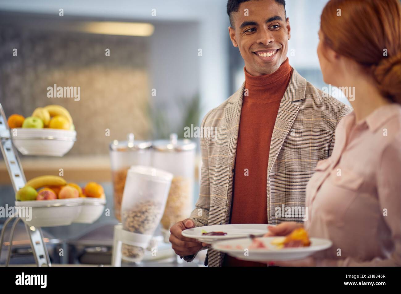 Two young colleagues are talking while helping themselves with a food ...