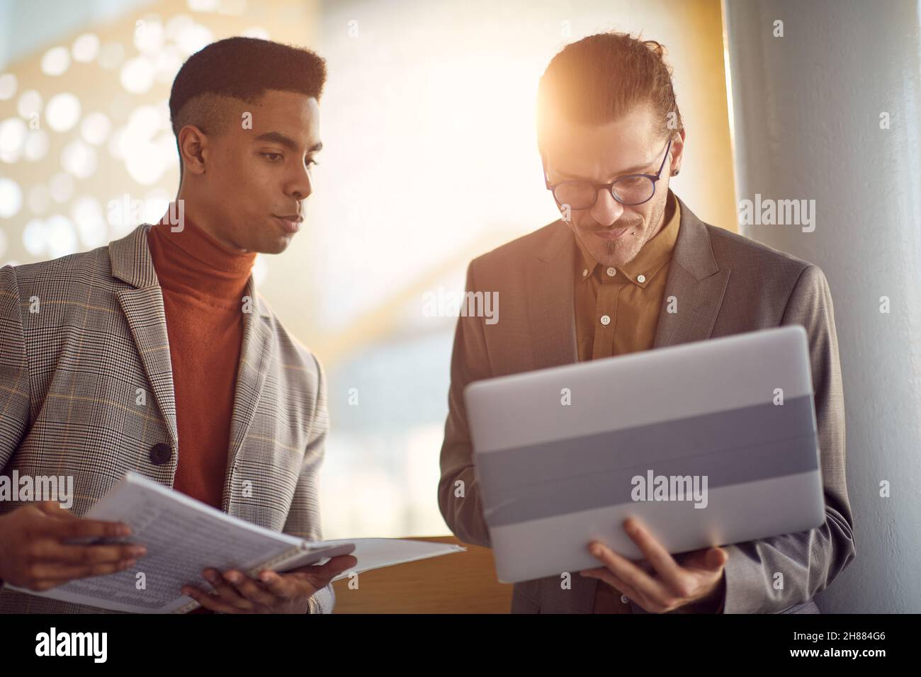 Two young businessmen are standing in the hallway and doing some work ...