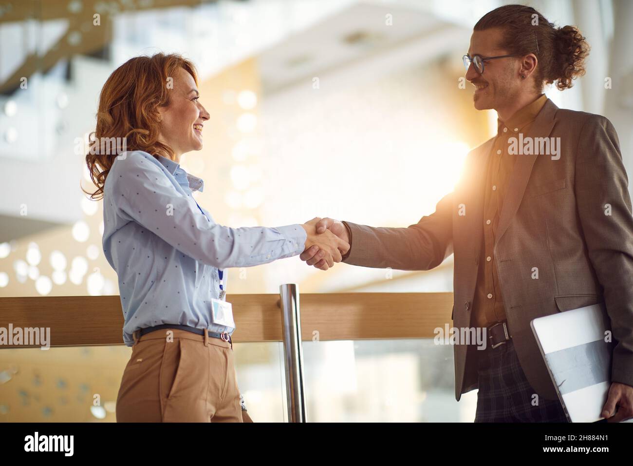 A female business manager is handshaking with her young male colleague ...
