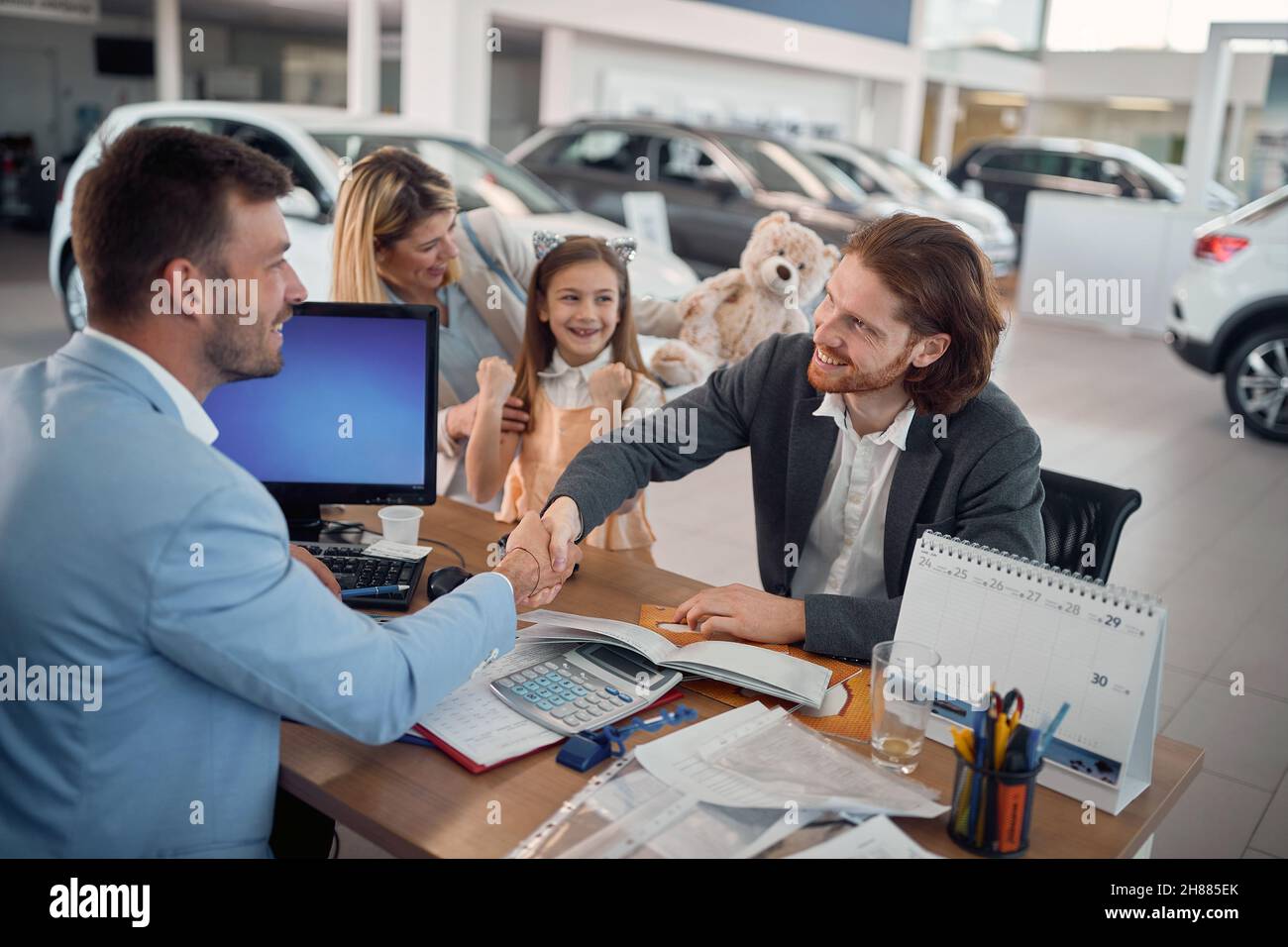 Young family shaking hands with sales agent after a successful new car ...
