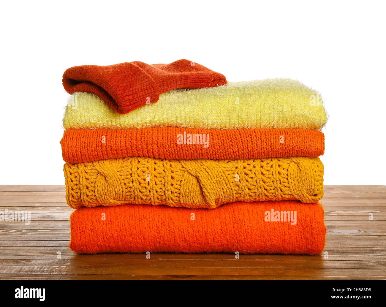 Stack of different stylish sweaters and hat on wooden table against ...
