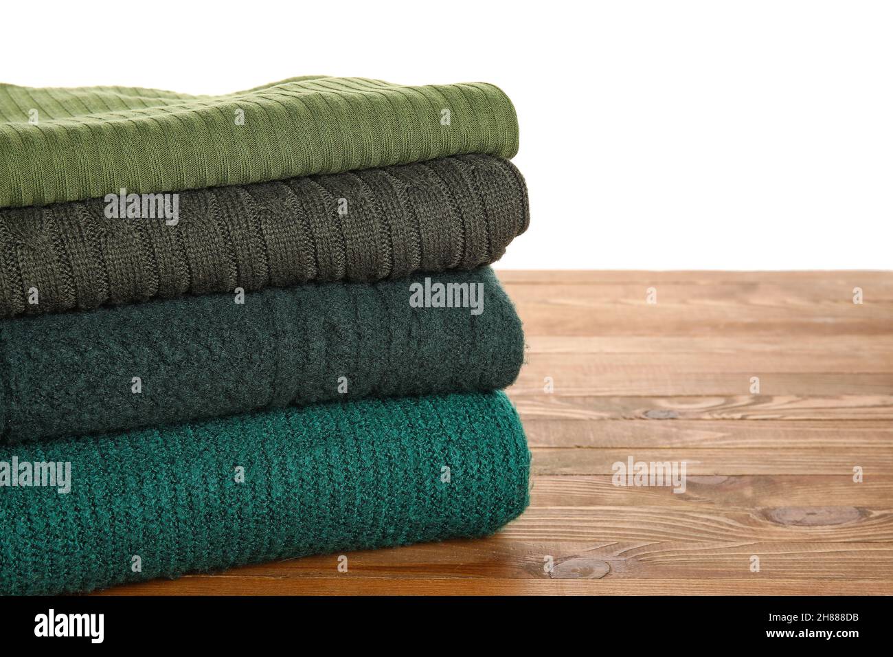 Stack of different green sweaters on wooden table against white ...
