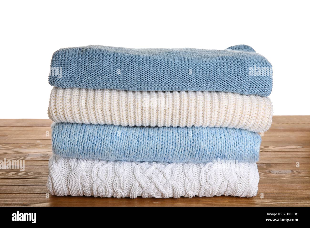 Different stylish sweaters on wooden table against white background ...