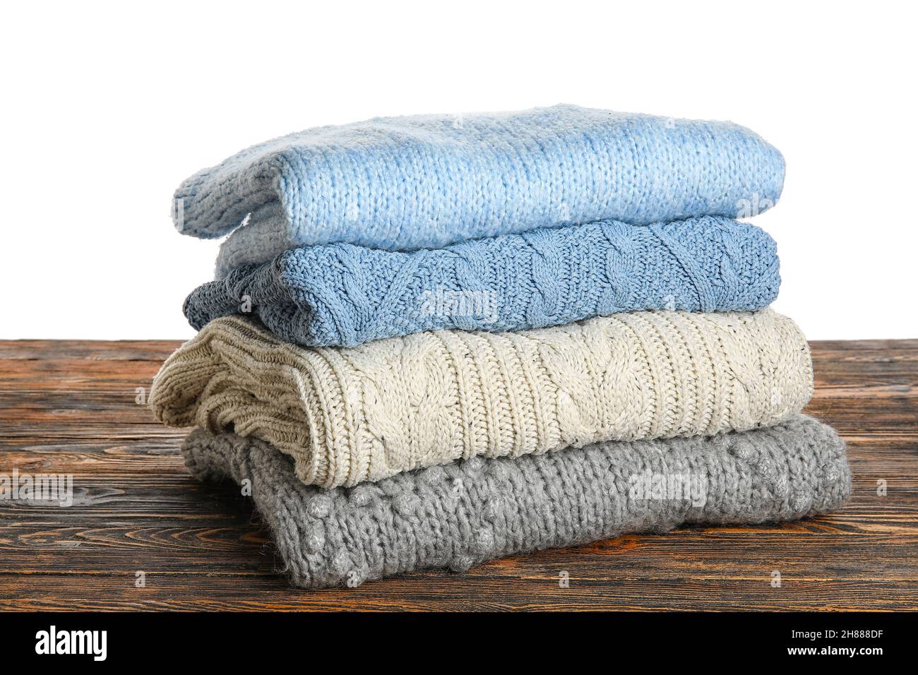 Stylish blue and grey sweaters on wooden table against white background ...