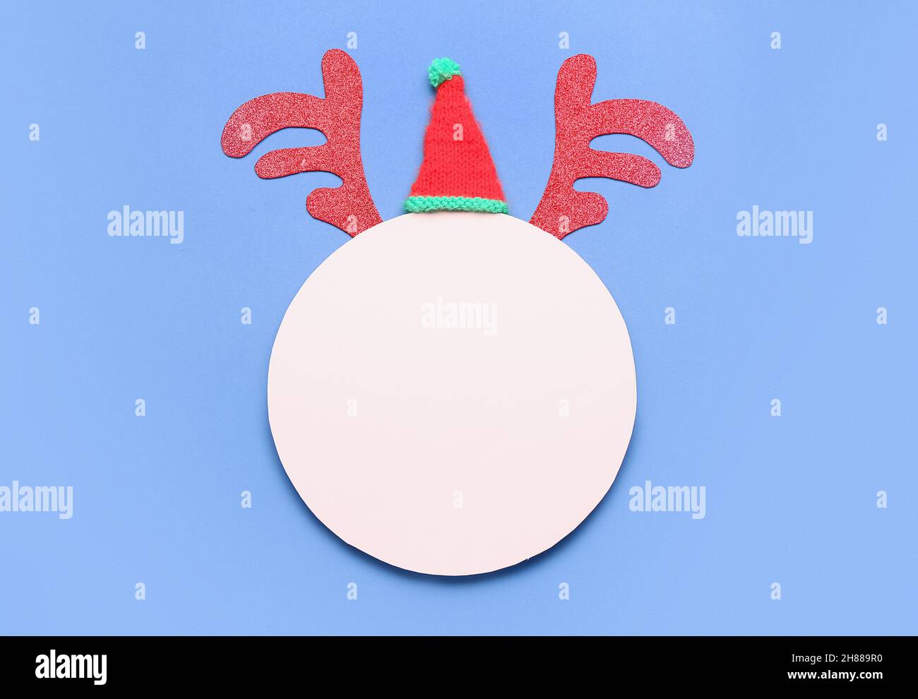 Blank card with cute reindeer horns and knitted hat on color background ...