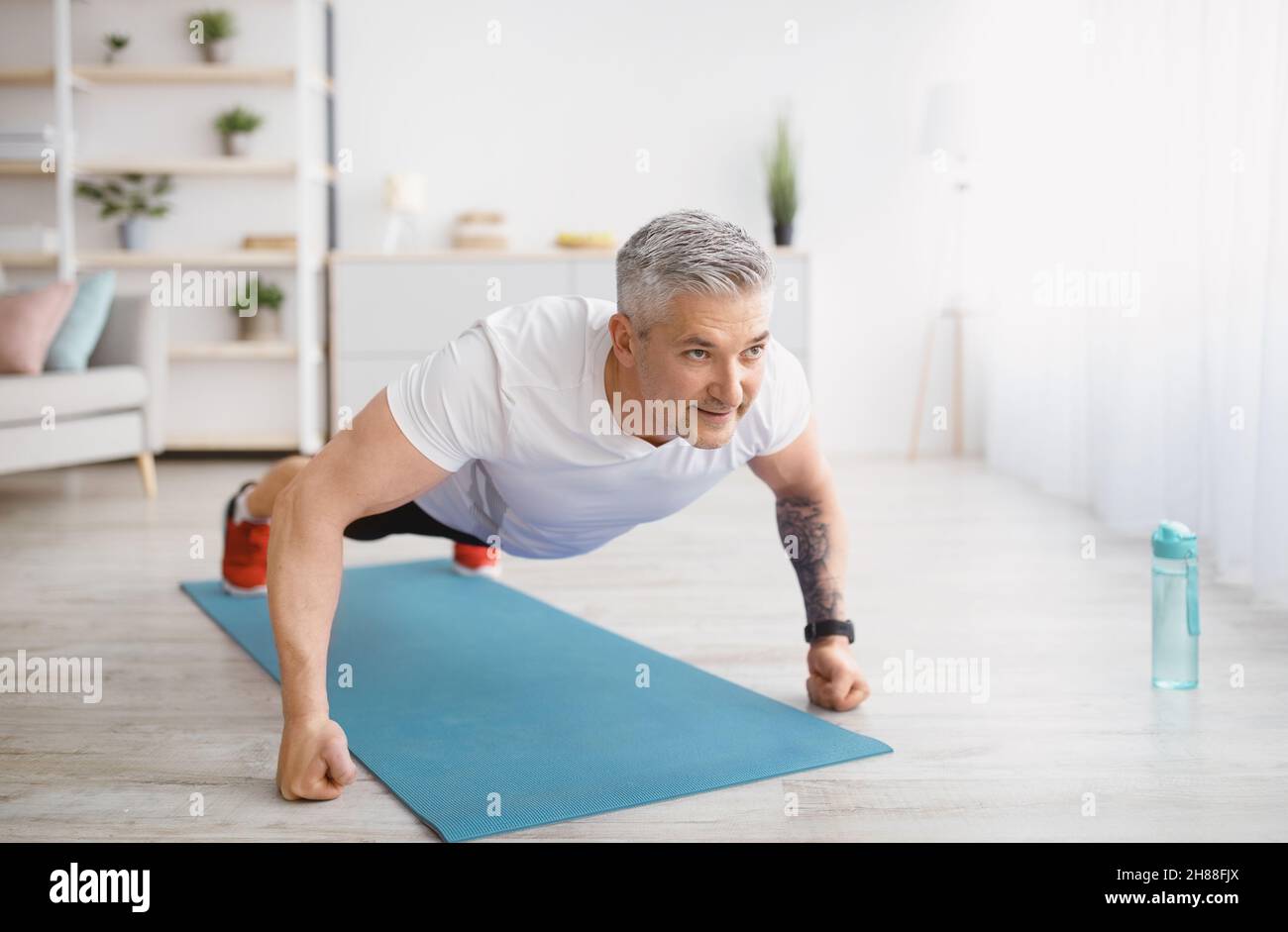 Strong senior man making strength workout, doing push ups on sports mat ...