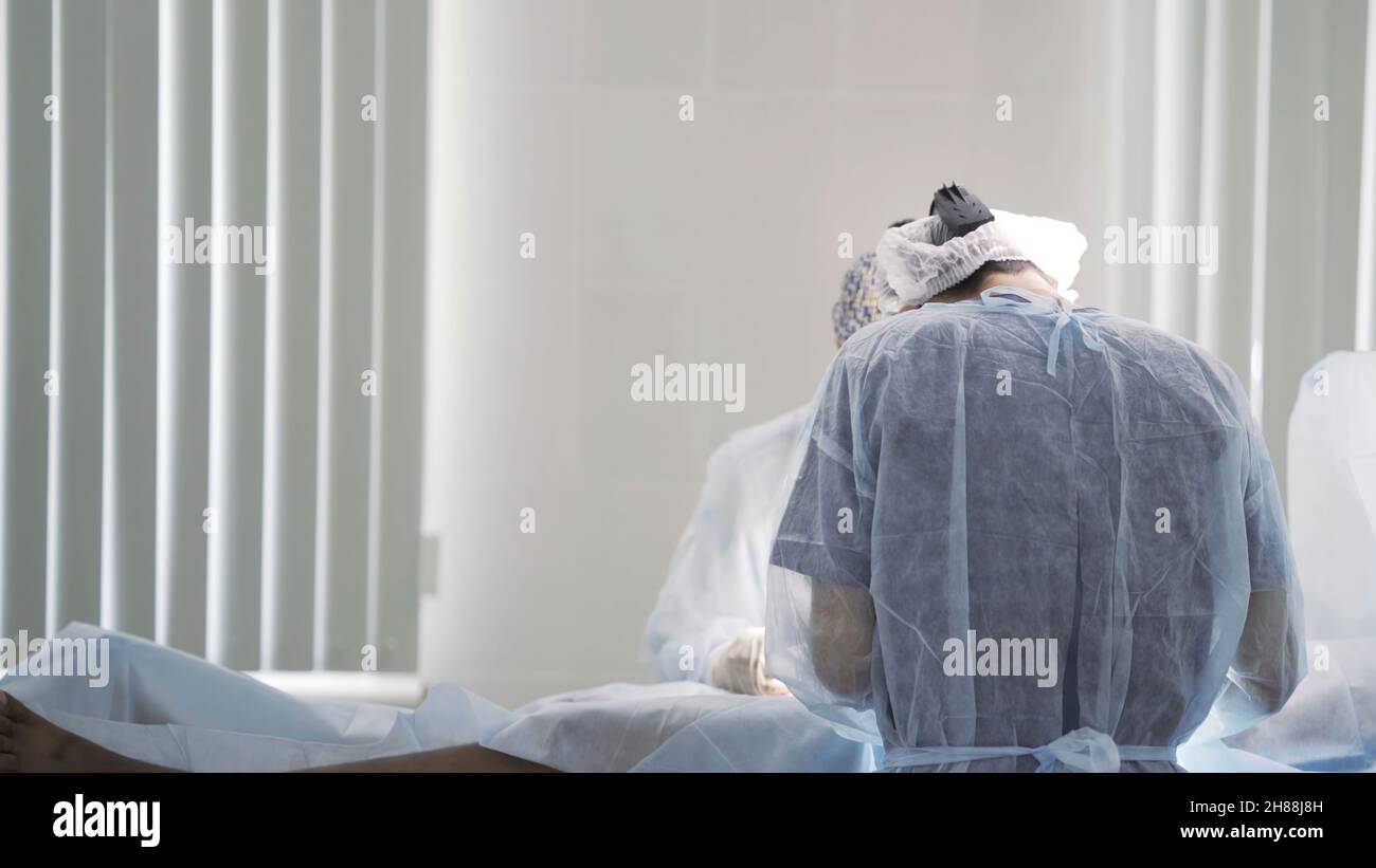 Rear view of a surgeon at work in operating room. Side view of a ...