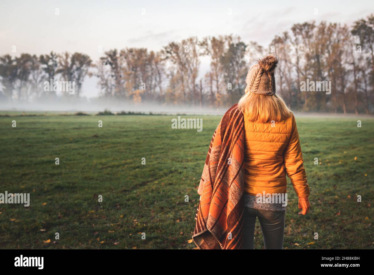 Cold autumn morning with fog. Woman with knit hat and blanket standing ...