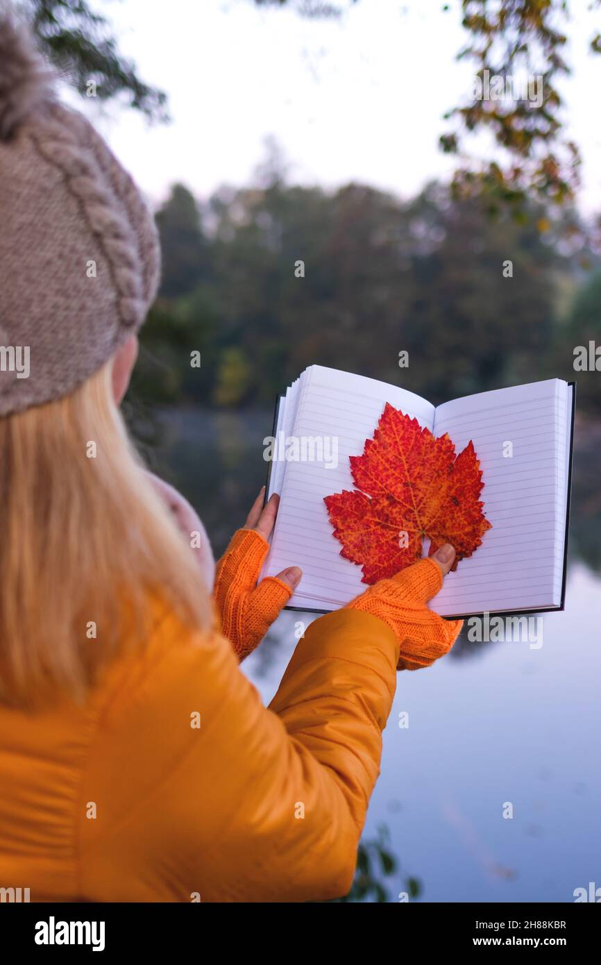 Autumn diary. Woman holding red leaf at open notepad. Changing seasons ...