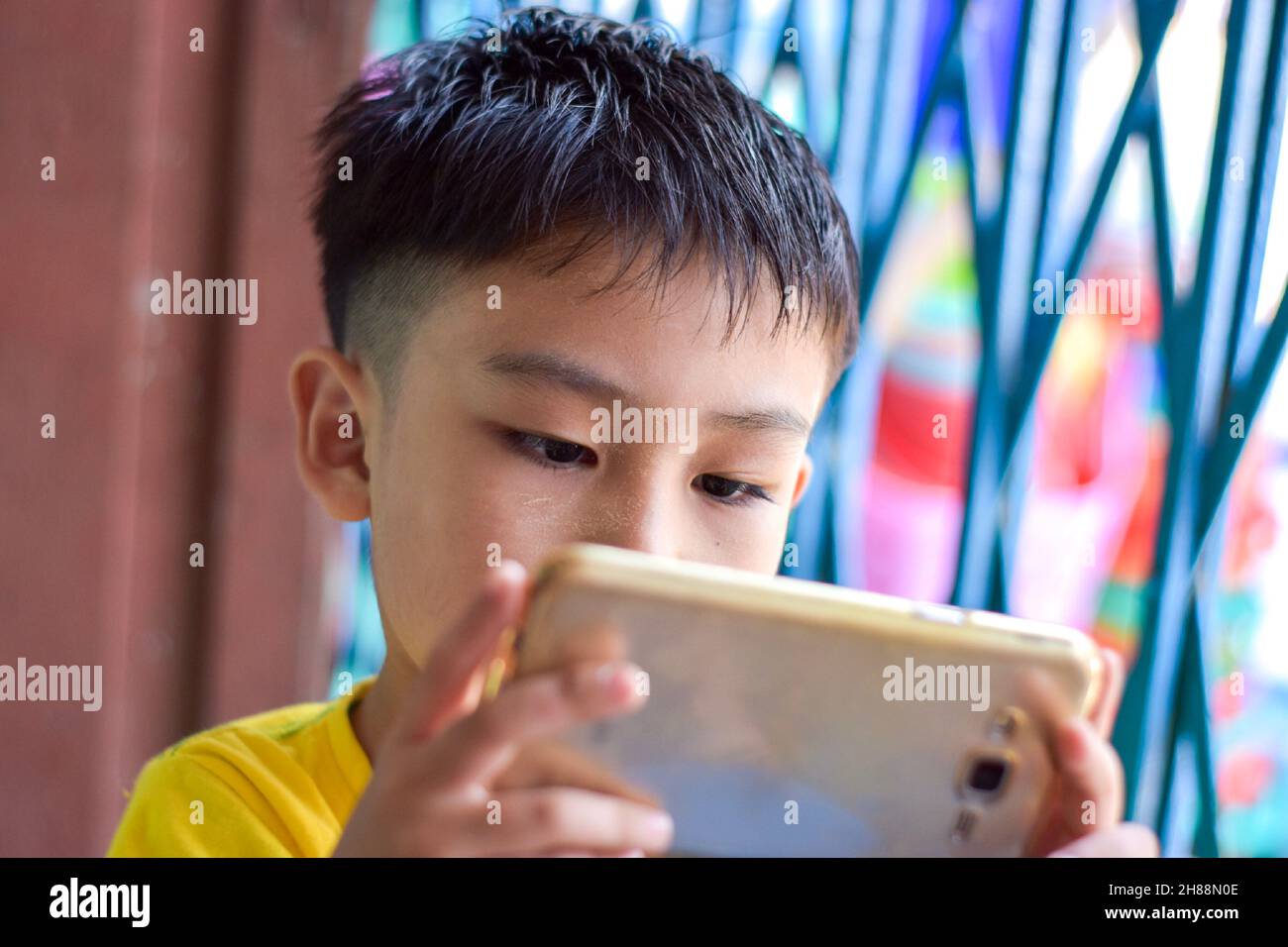 Asian child with squint eyes playing mobile game with smartphone ...