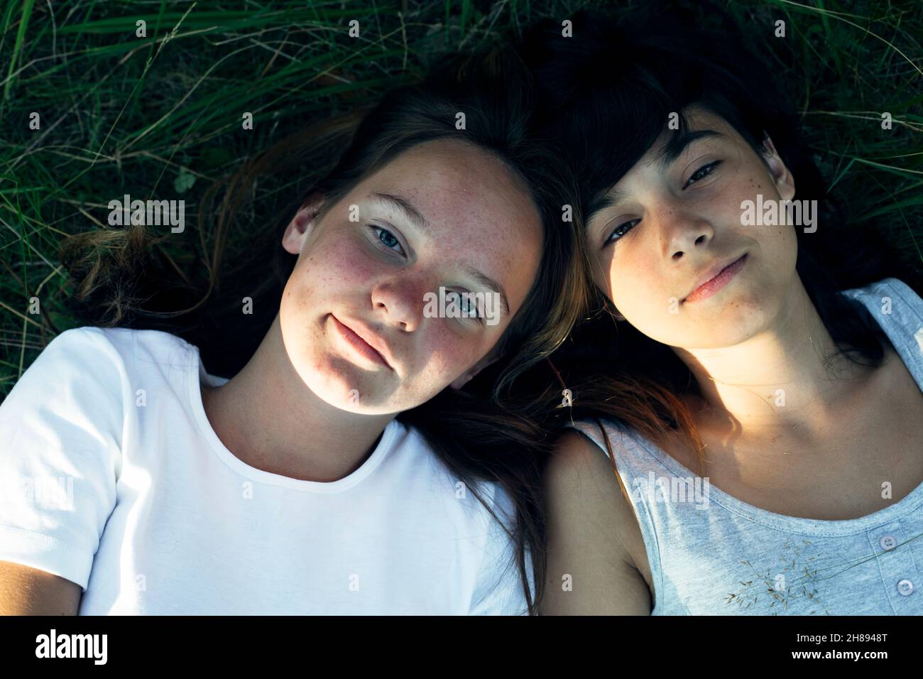 Portrait from above of two girls girlfriends lying on the green grass ...