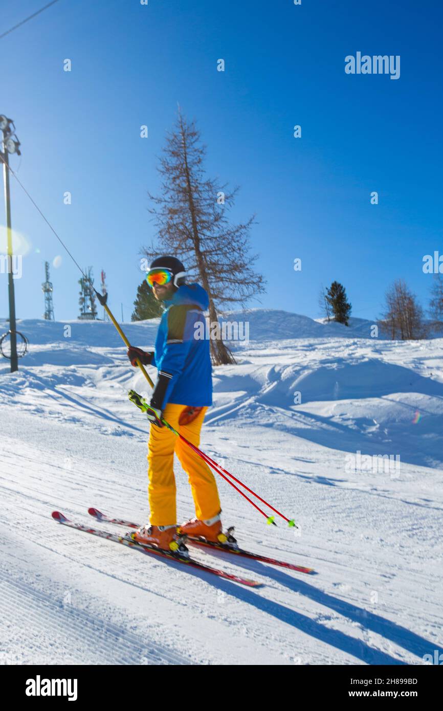 Alpine skier with T-bar lift, blue and yellow clothes on slope with ...