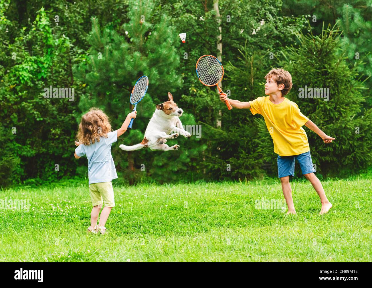 Kids having fun playing badminton and dog jumping up to catch and steal ...