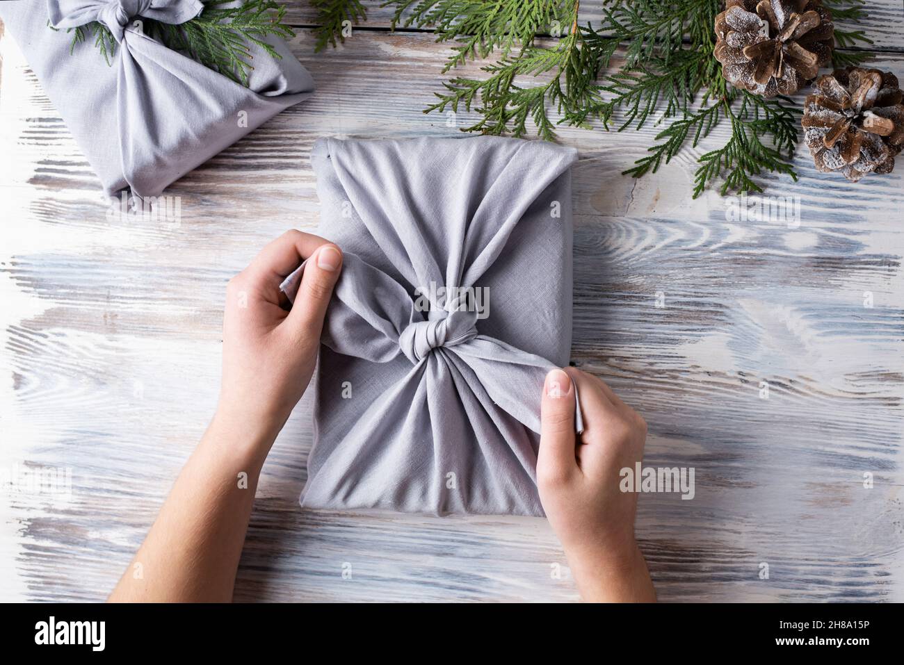 Female hands wrapping a Christmas present in a reusable gray cloth on a ...